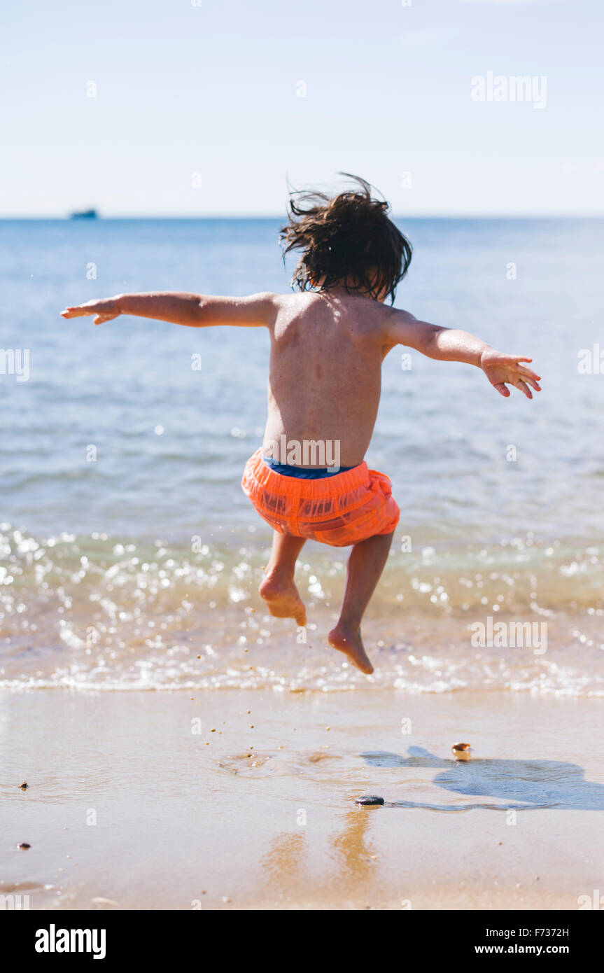 A boy in swimming trunks jumping over waves on the sea shore Stock ...