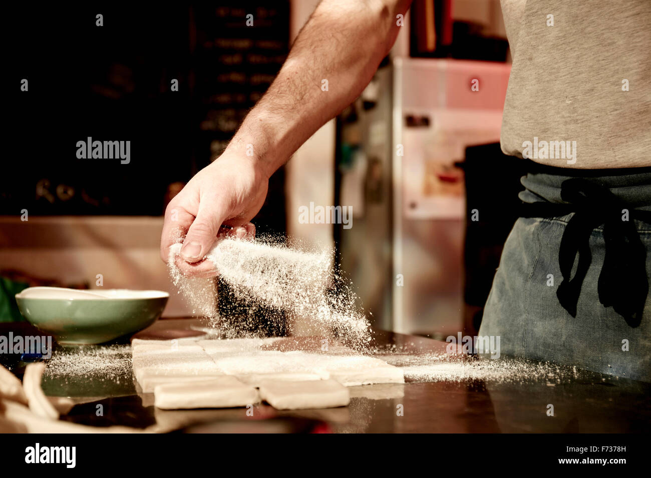 A baker working on a floured surface, dividing prepared dough into ...
