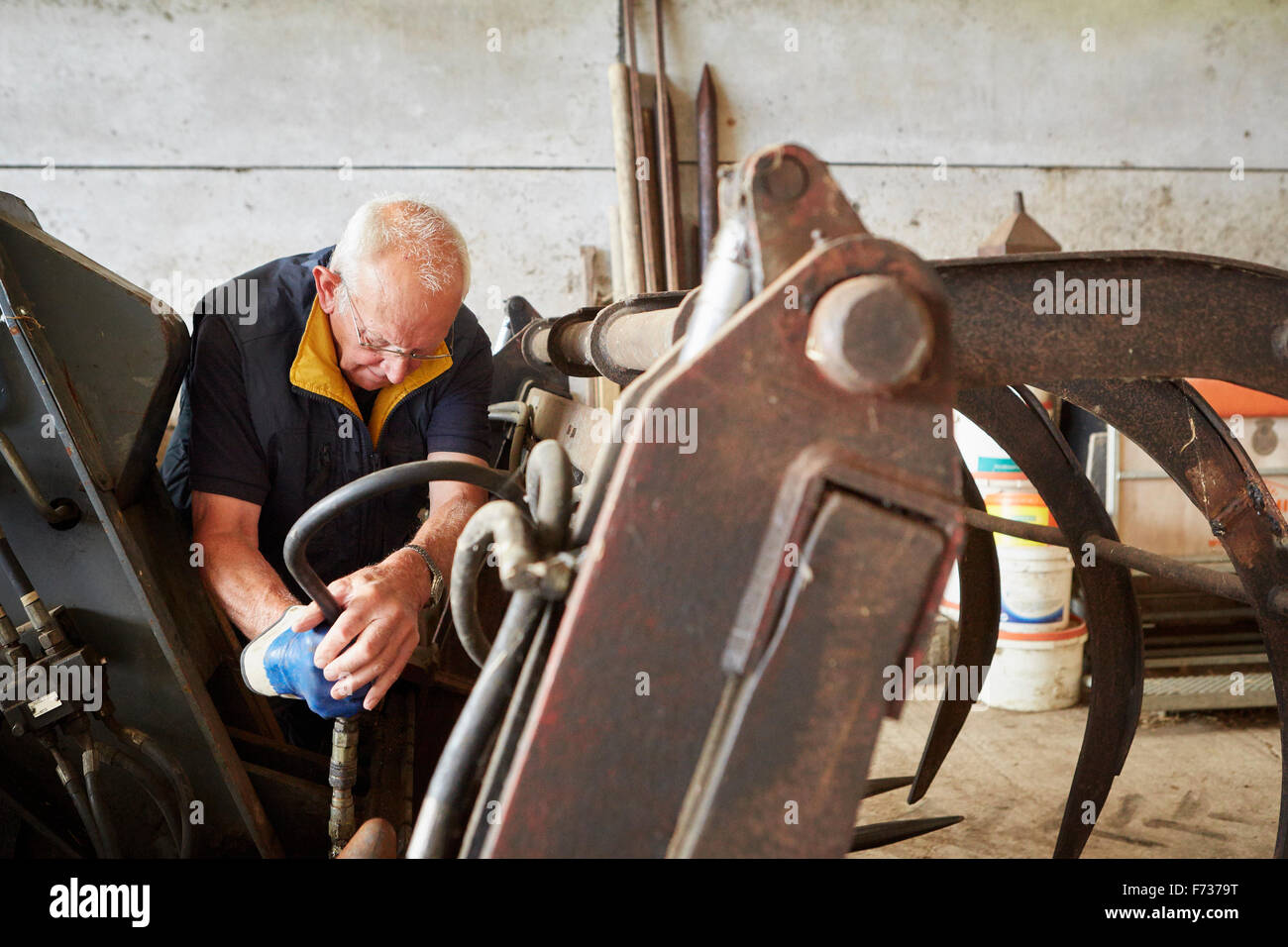 A man working with tools on farm machinery in a barn Stock Photo - Alamy