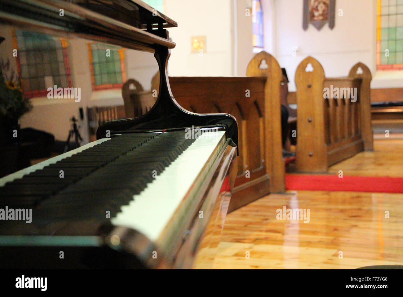 Close-up of a black grand piano in a church, with church pews in the ...