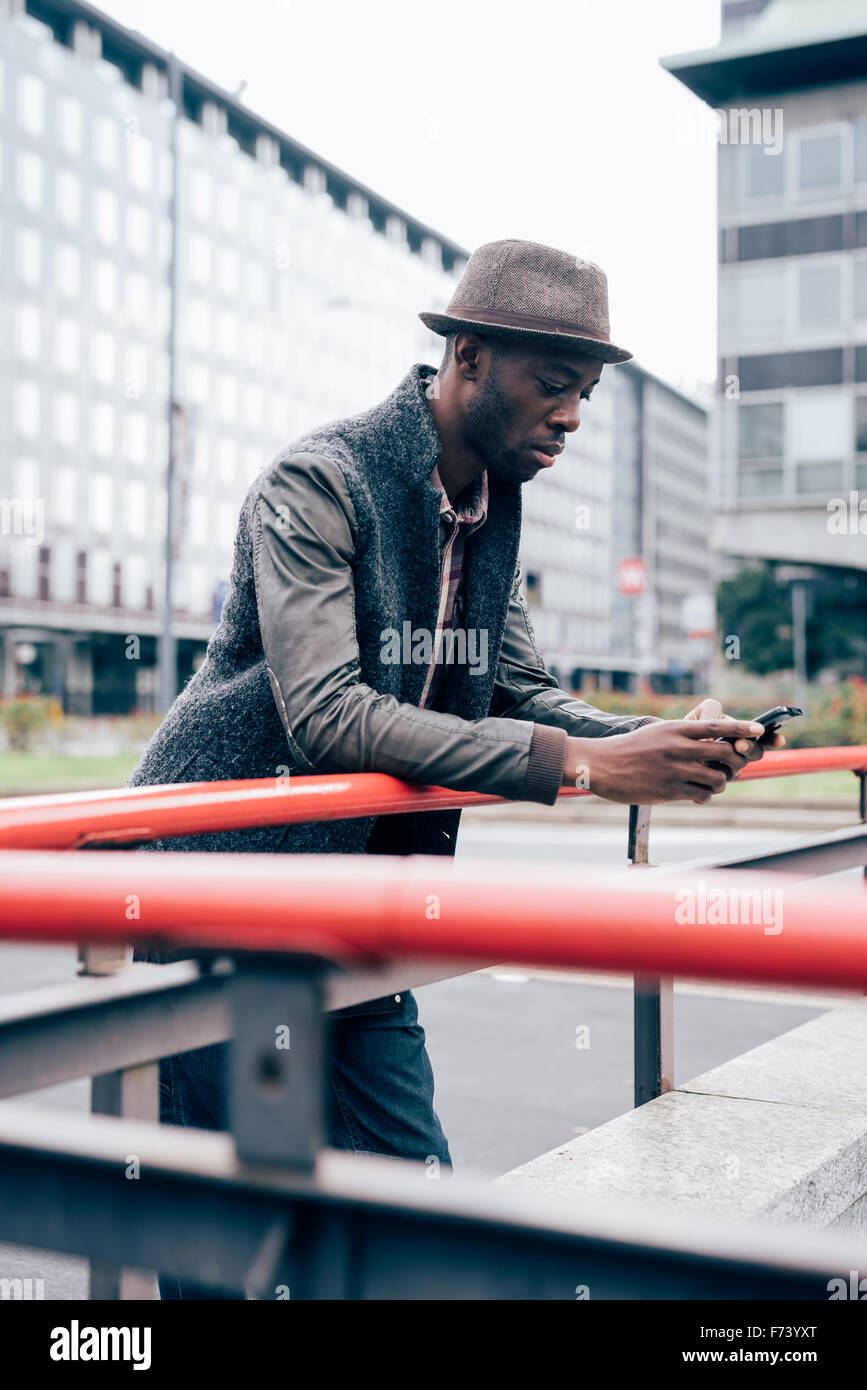 Knee figure of young handsome afro black man leaning on a handrail, holding a smartphone ...