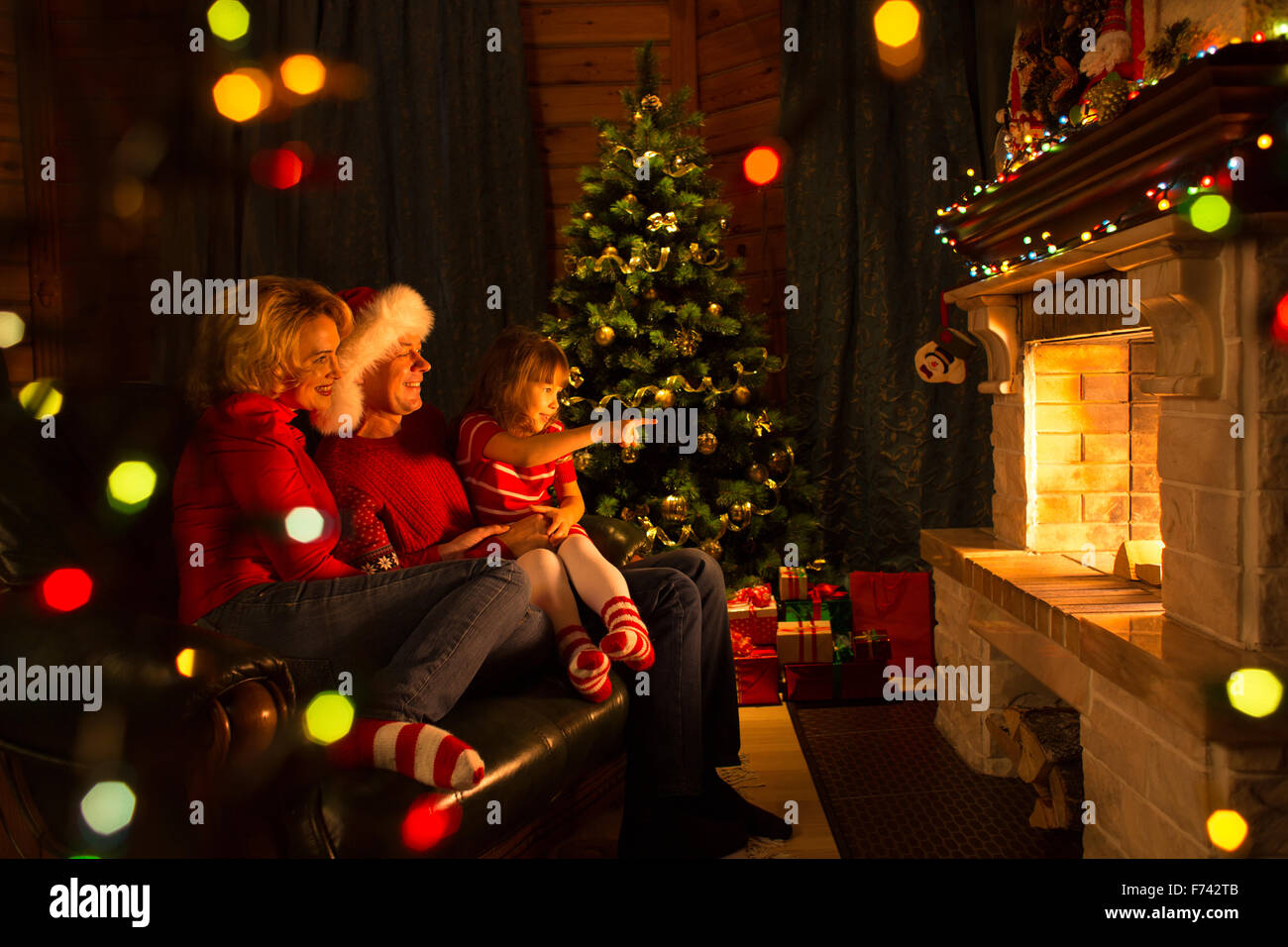 Happy family sitting by fire place at Christmas tree Stock Photo - Alamy
