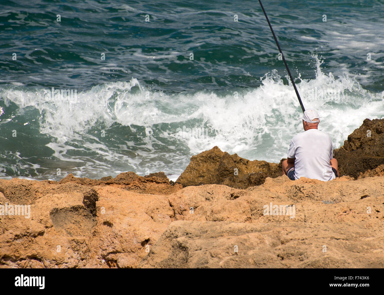 Man fishing on rocks by the sea Stock Photo - Alamy