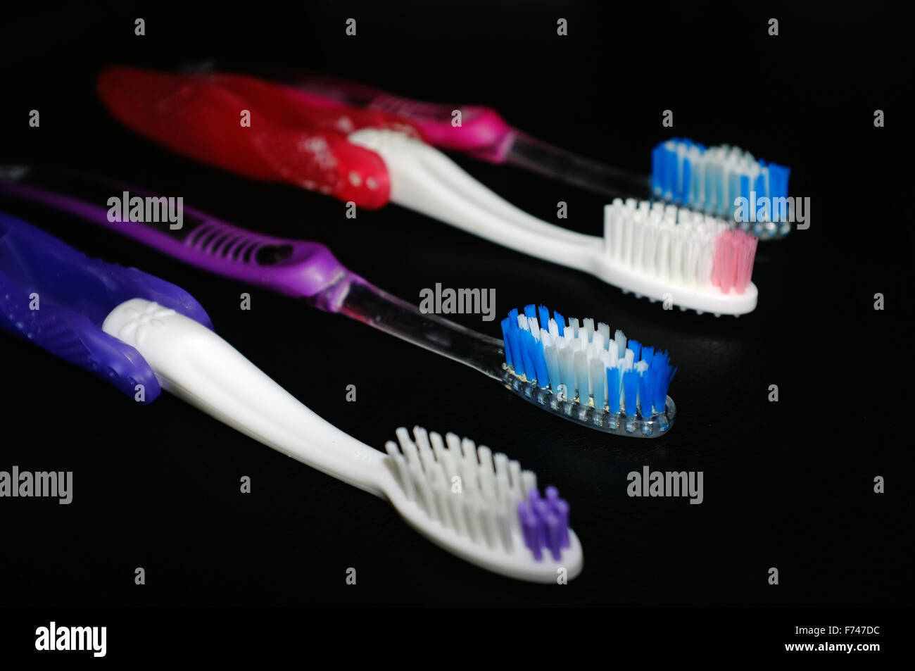 A row of four toothbrush heads photographed against a black background ...
