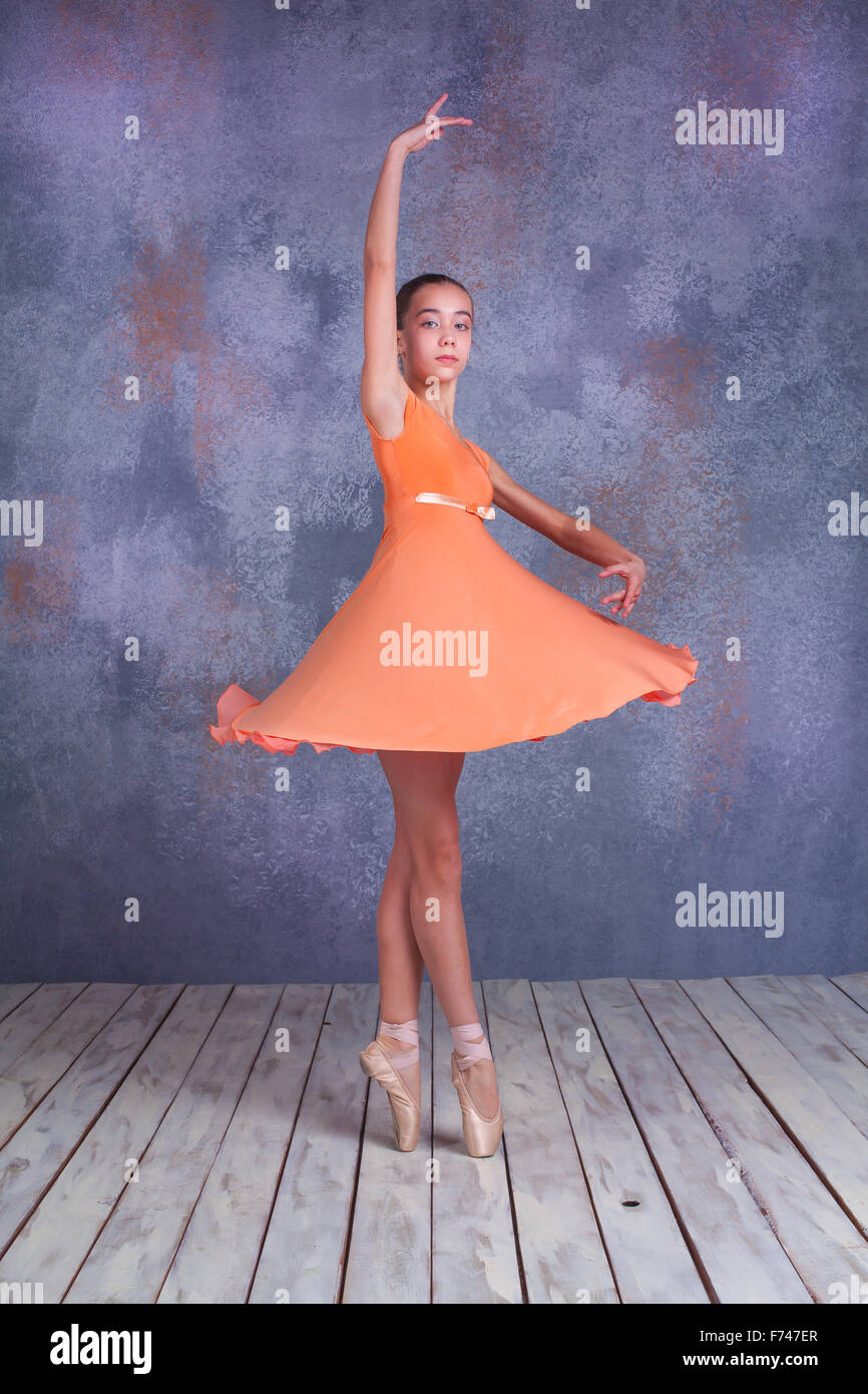 The young ballerina in orange dress dancing in studio on gray ...
