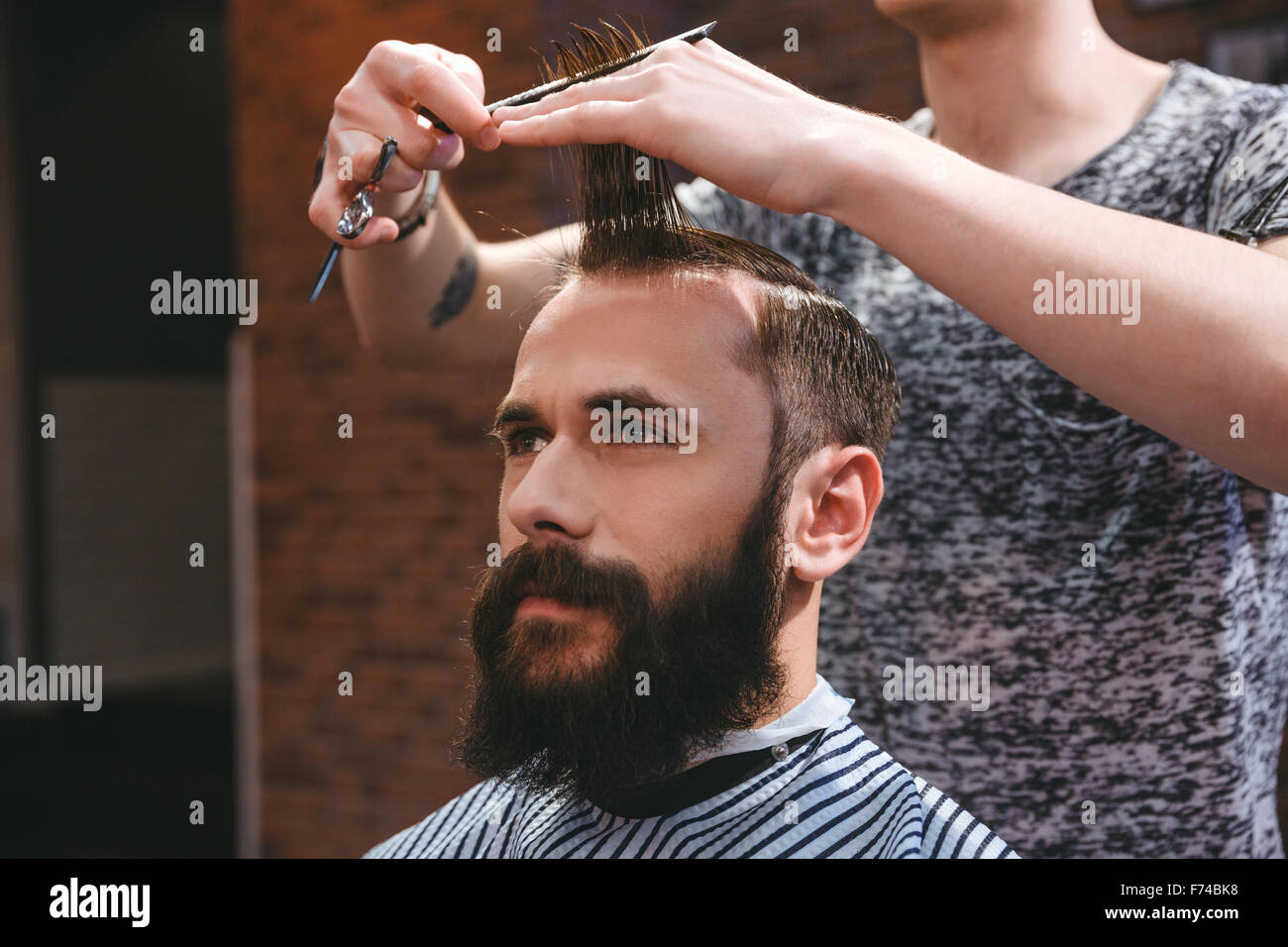 Portrait of young handsome man with beard having a haircut with comb ...