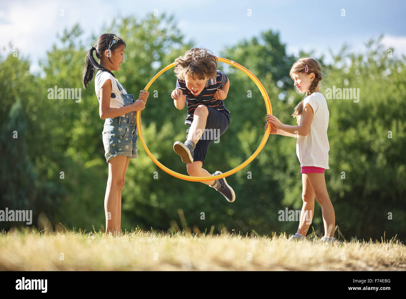Boy jumps through hula hoop while two girls are holding it Stock Photo ...