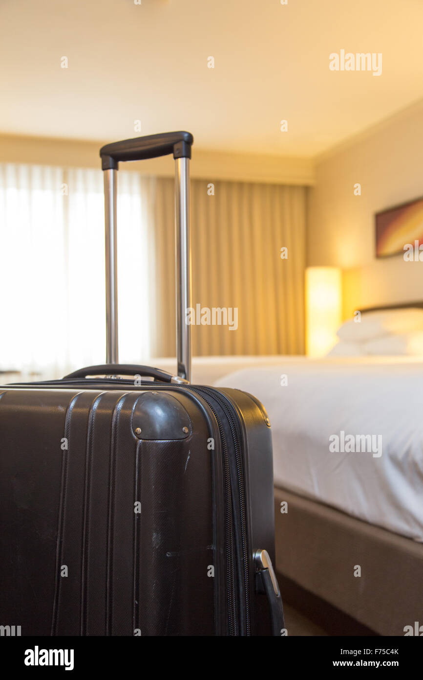 a hard sided black suitcase in focus, with a hotel room in the ...