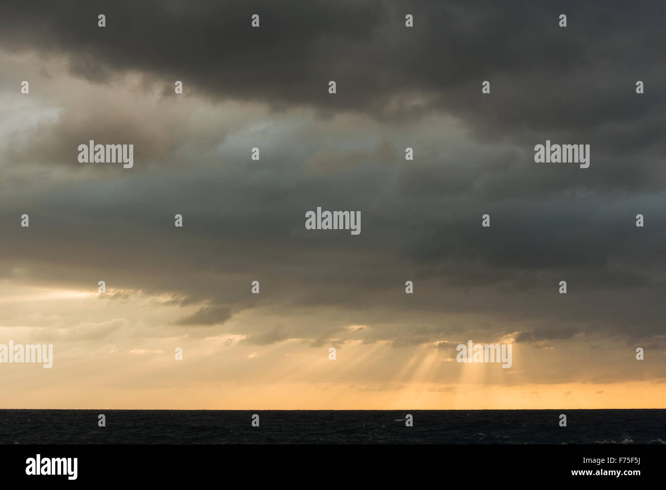 Sunrise cloudscape with orange light and sun rays from behind heavy ...