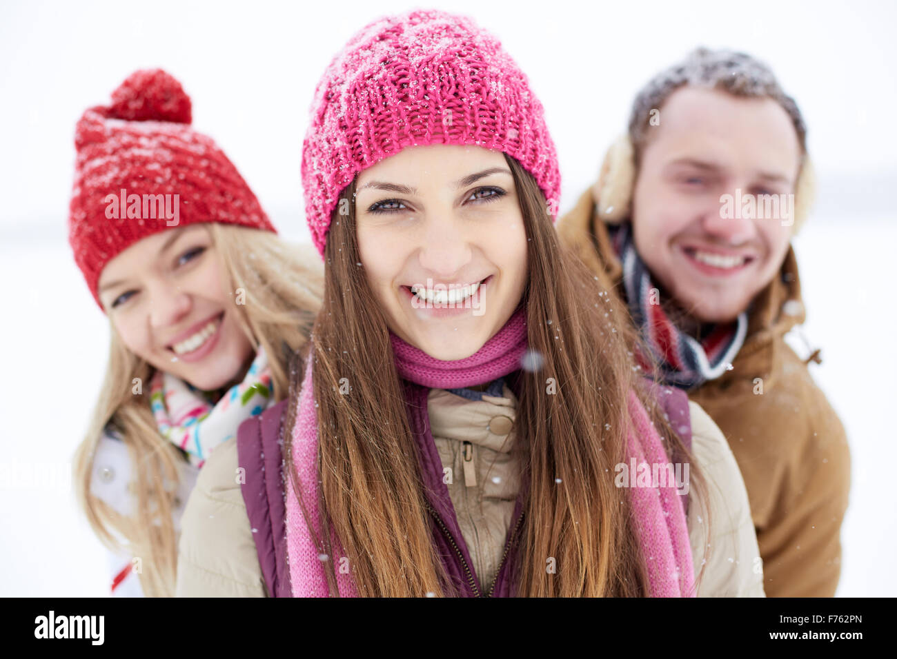 Happy friends in winterwear looking at camera during snowfall Stock ...