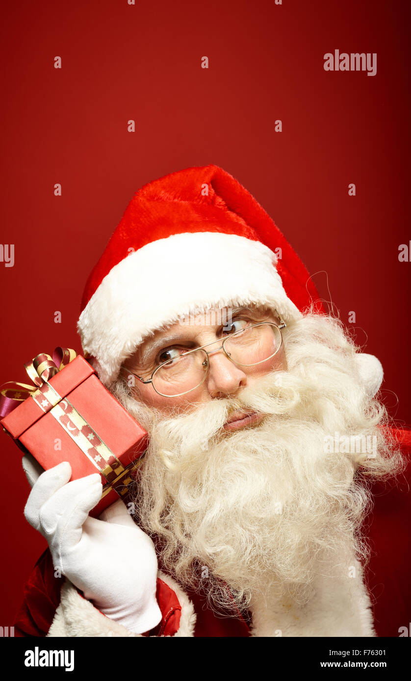 Curious Santa with small gift-box by his ear Stock Photo - Alamy