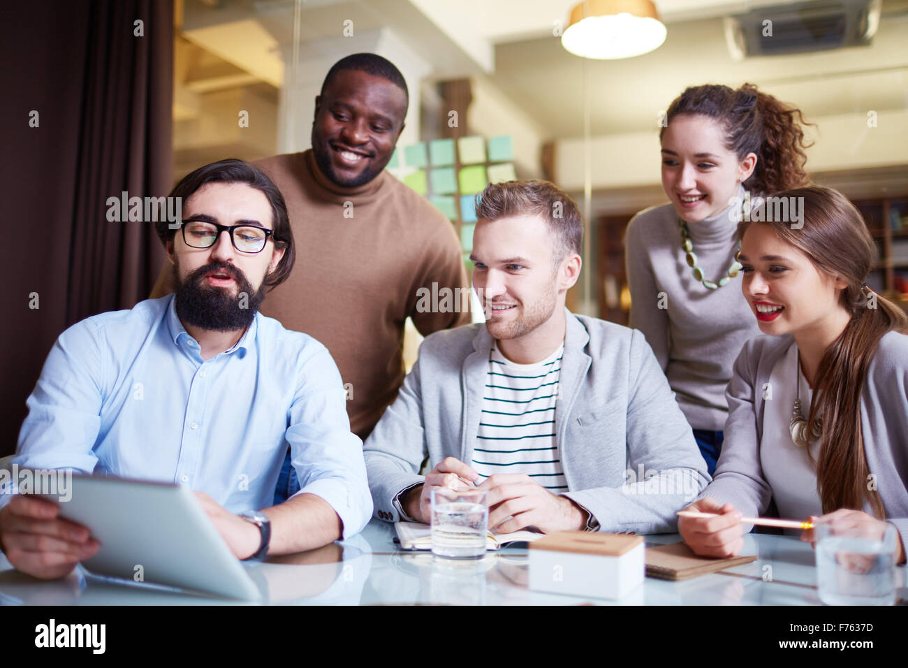 Young employees looking at touchpad screen while their colleague ...