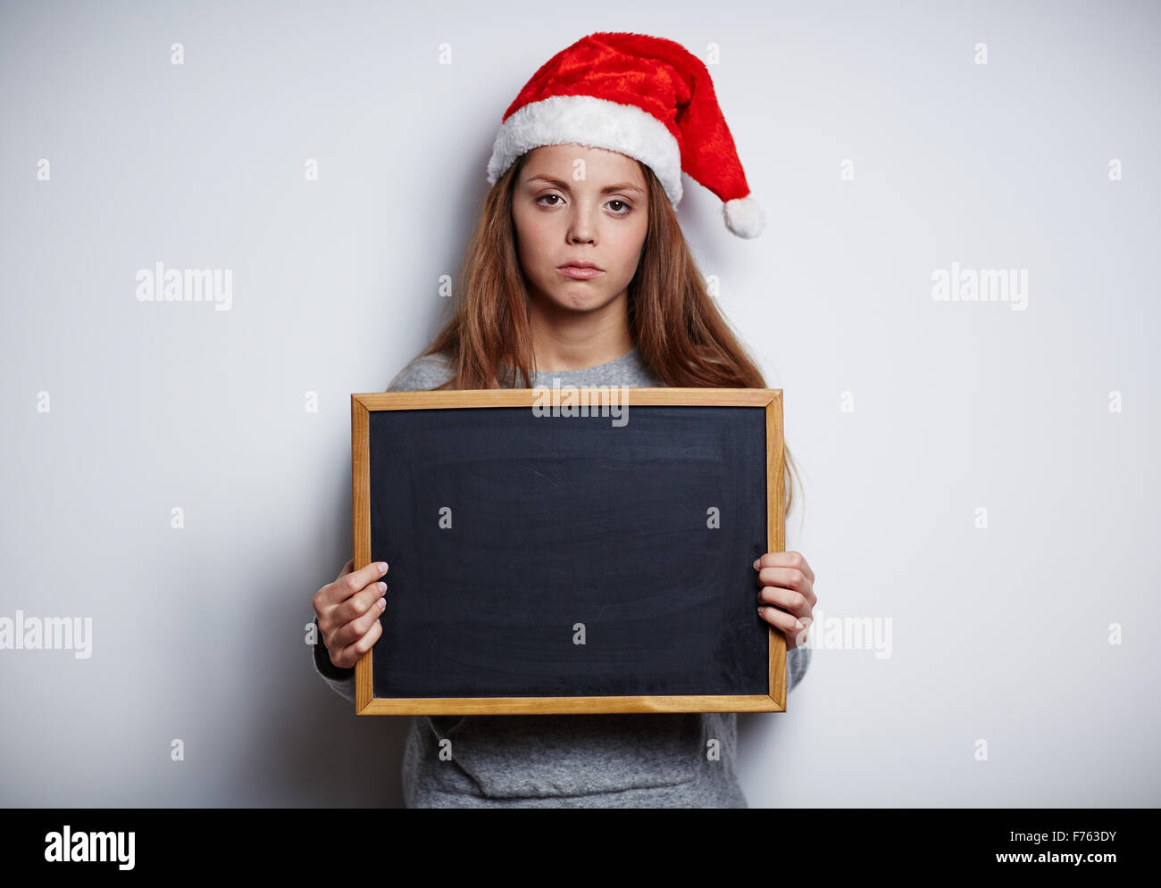 Sulky girl in Santa cap showing empty blackboard Stock Photo - Alamy