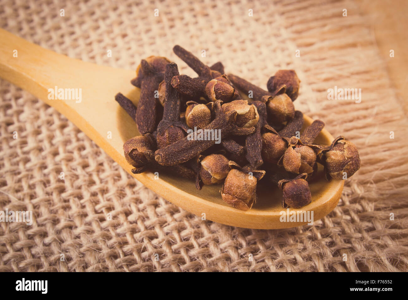 Vintage photo, Heap of brown cloves on wooden spoon lying on jute ...