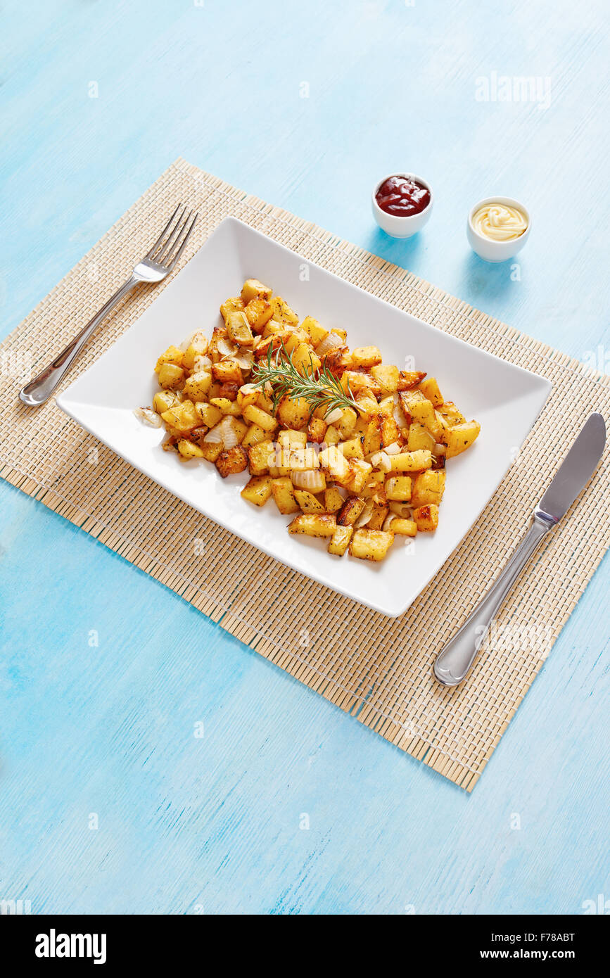 Roasted potatoes on square white plate, fork, knife, sauces and blue ...