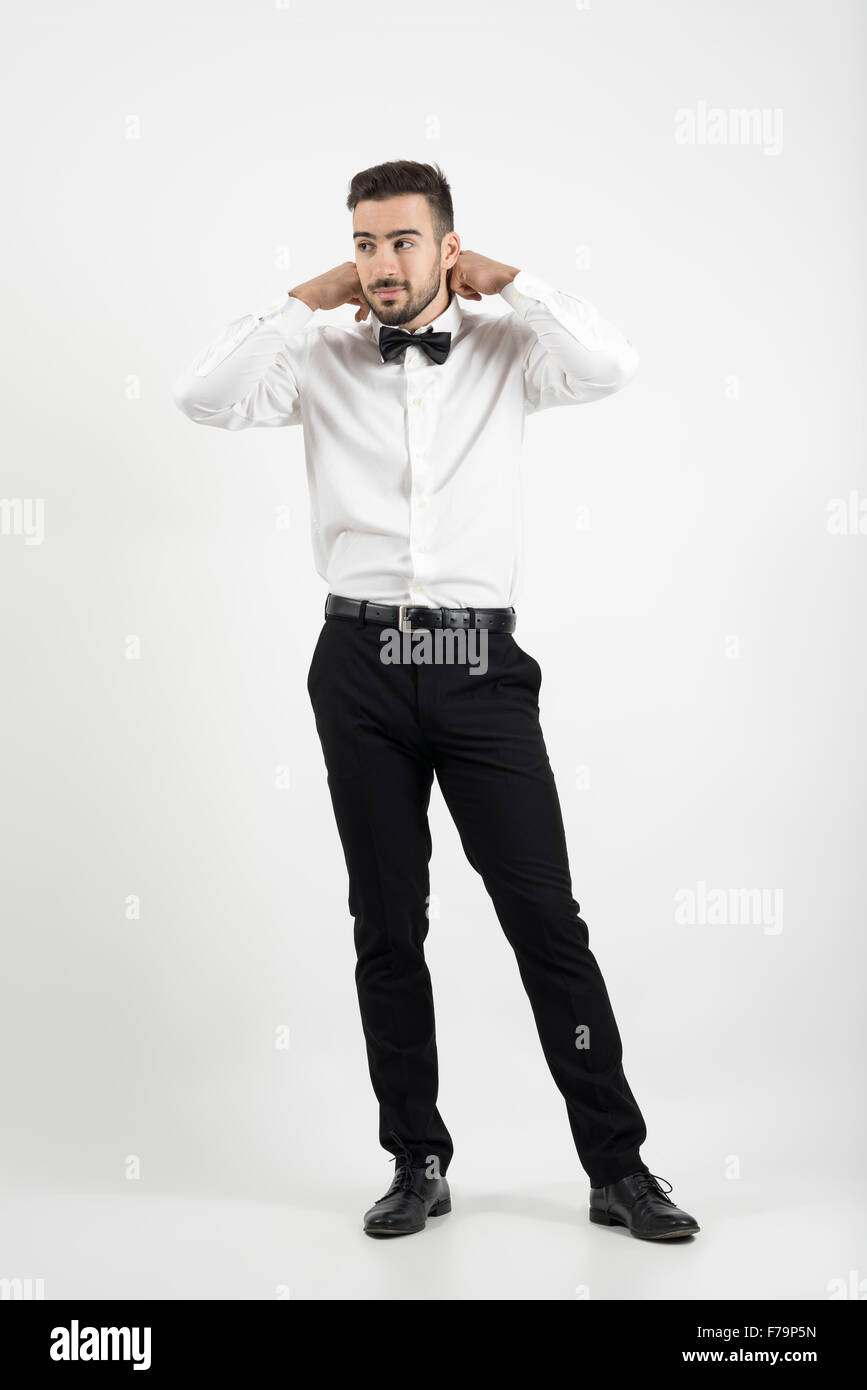 Young groom getting dressed adjusting bow tie looking away. Full body ...