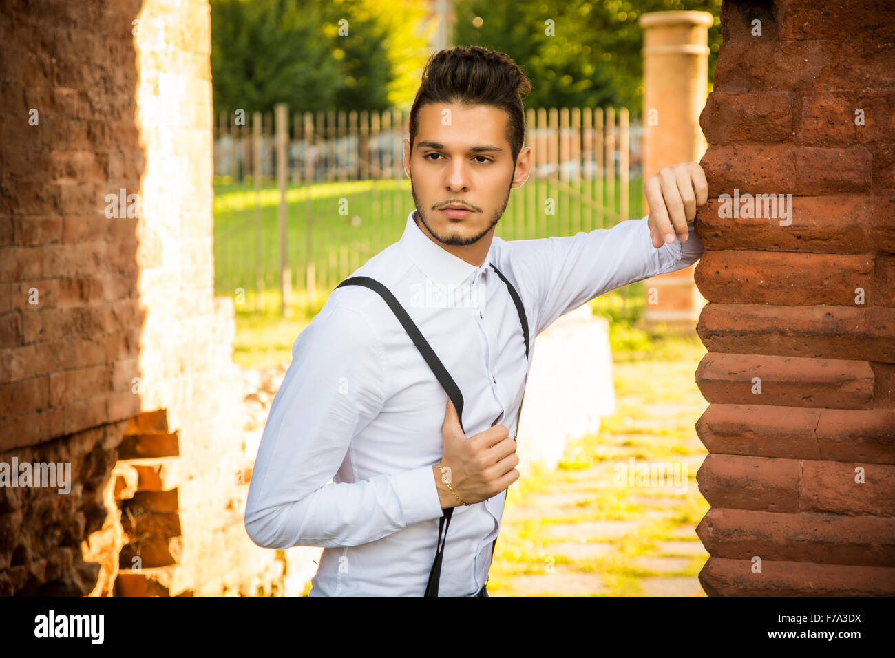 Portrait of young man leaning against a wall while standing outside. hi ...