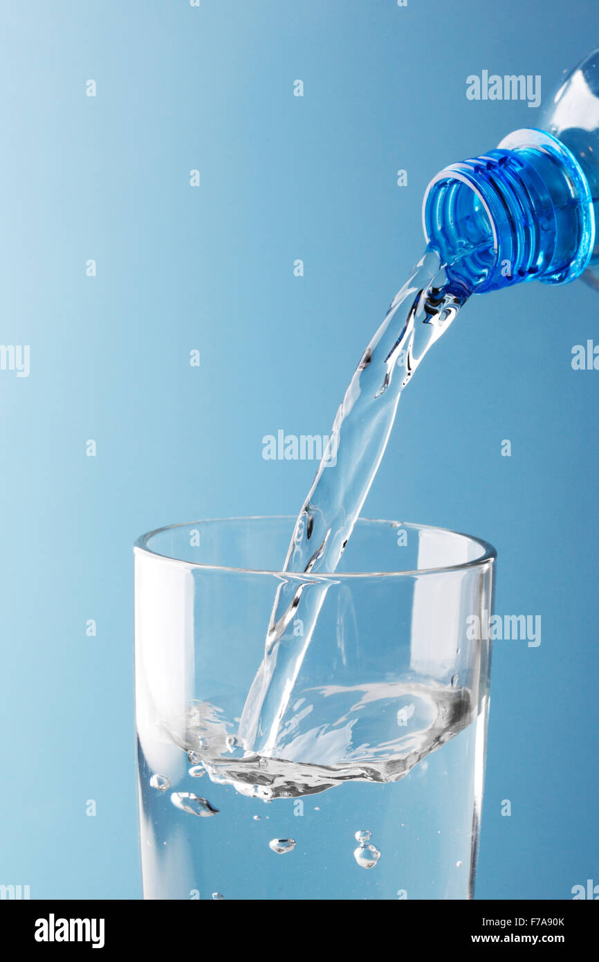Pouring water from plastic bottle into glass on blue background Stock Photo - Alamy