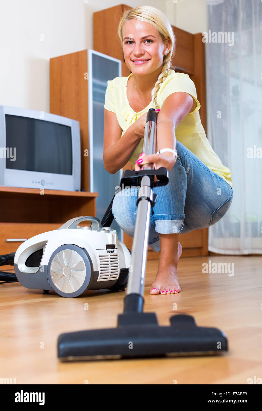 Positive blonde girl hoovering in living room and smiling Stock Photo ...