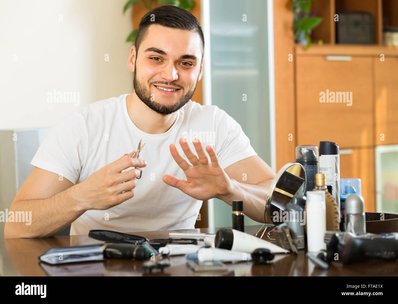Handsome smiling young guy cutting nails with cuticle scissors Stock ...