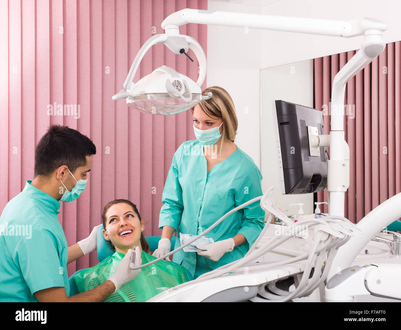 Smiling female patient and dentist with his assistant during check up ...