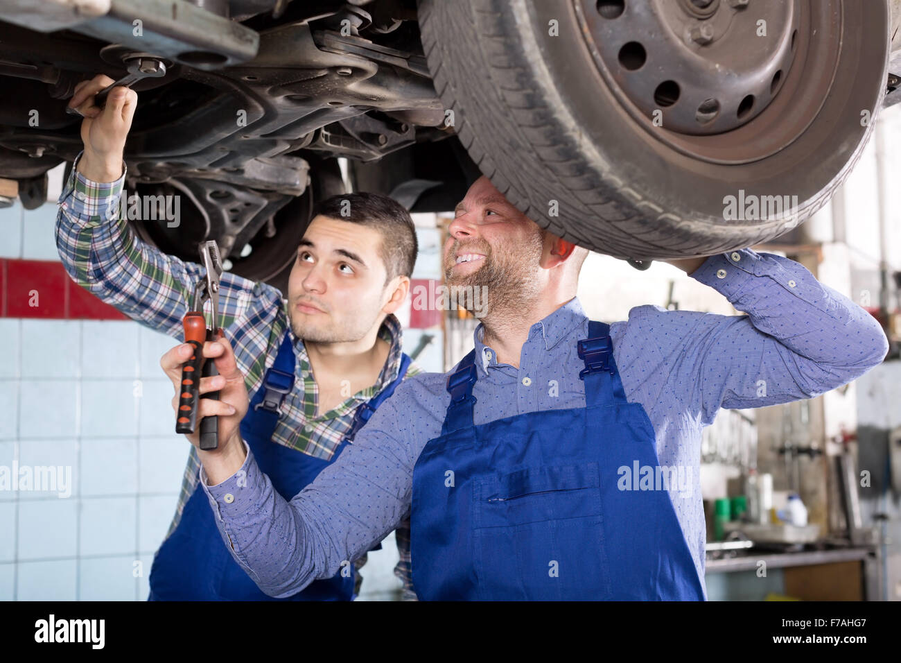 portrait happy two men in coveralls working at auto repair shop. Focus ...