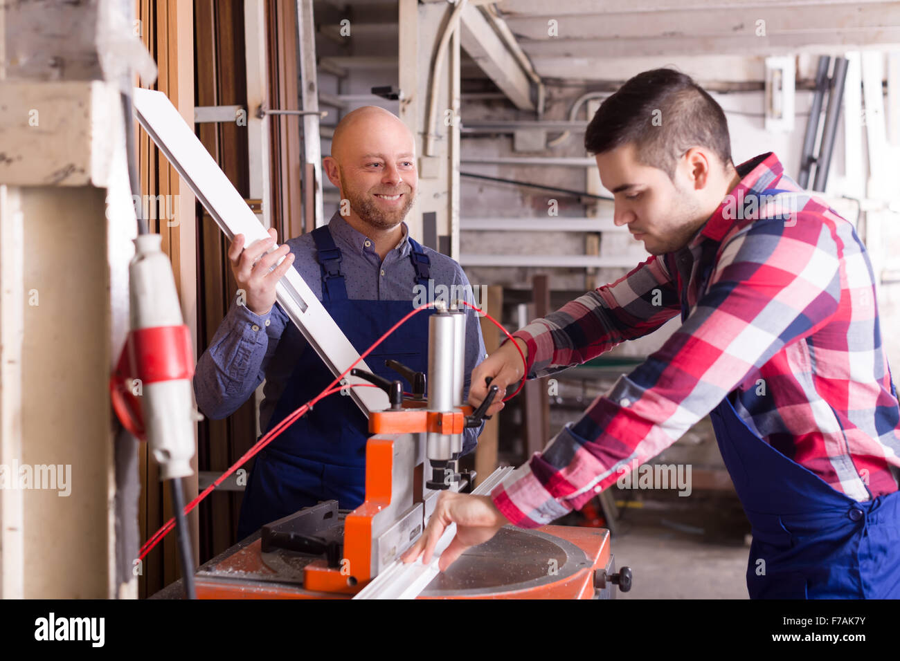 Two smiling workmen in uniform working on a machine in PVC shop Stock ...