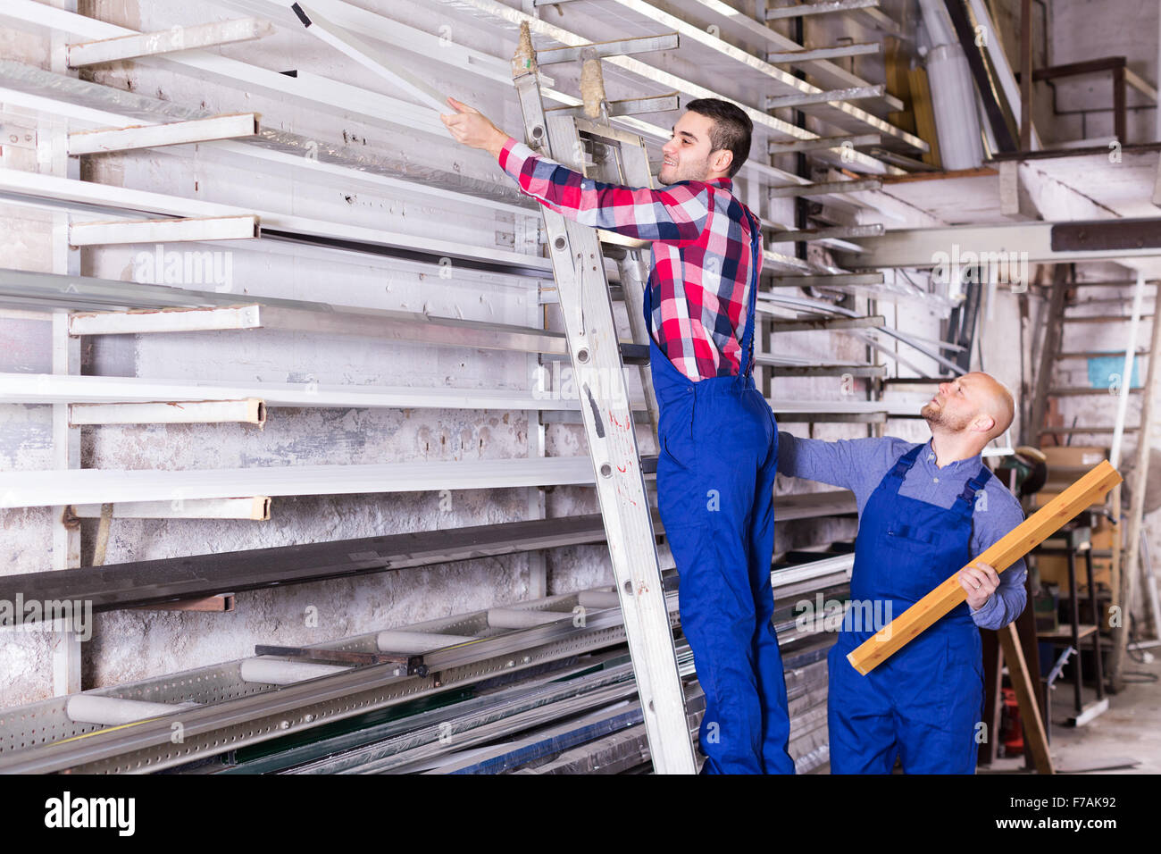Couple of workmen on step-ladder inspecting window frames at factory ...