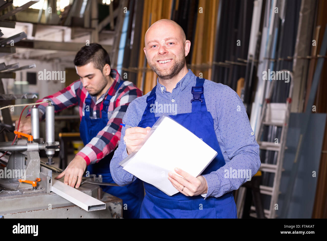 Careful worker operating in lathe, his boss with papers nearby Stock ...