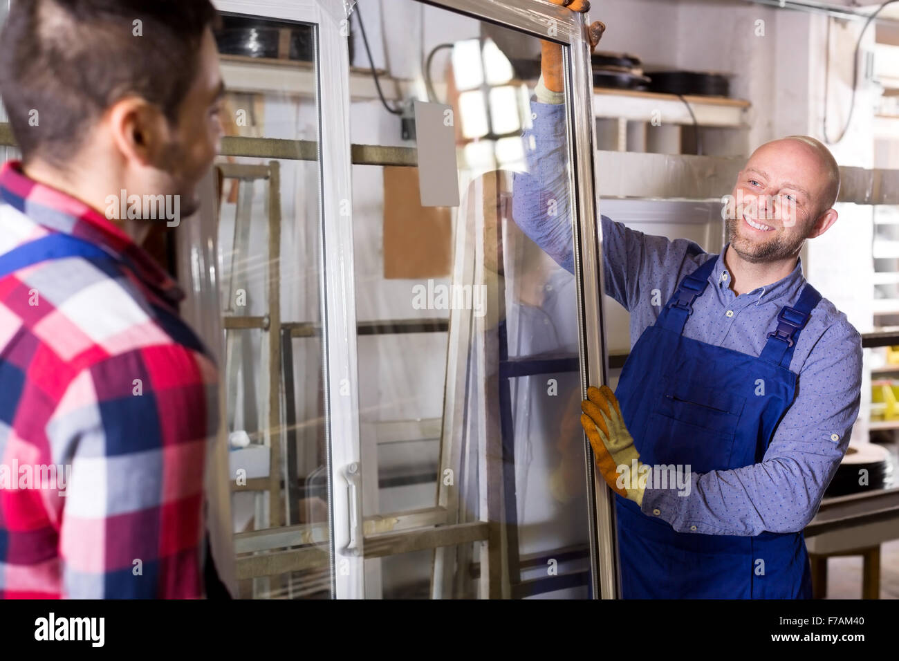 Two adult workmen in blue overalls with windows production at modern ...