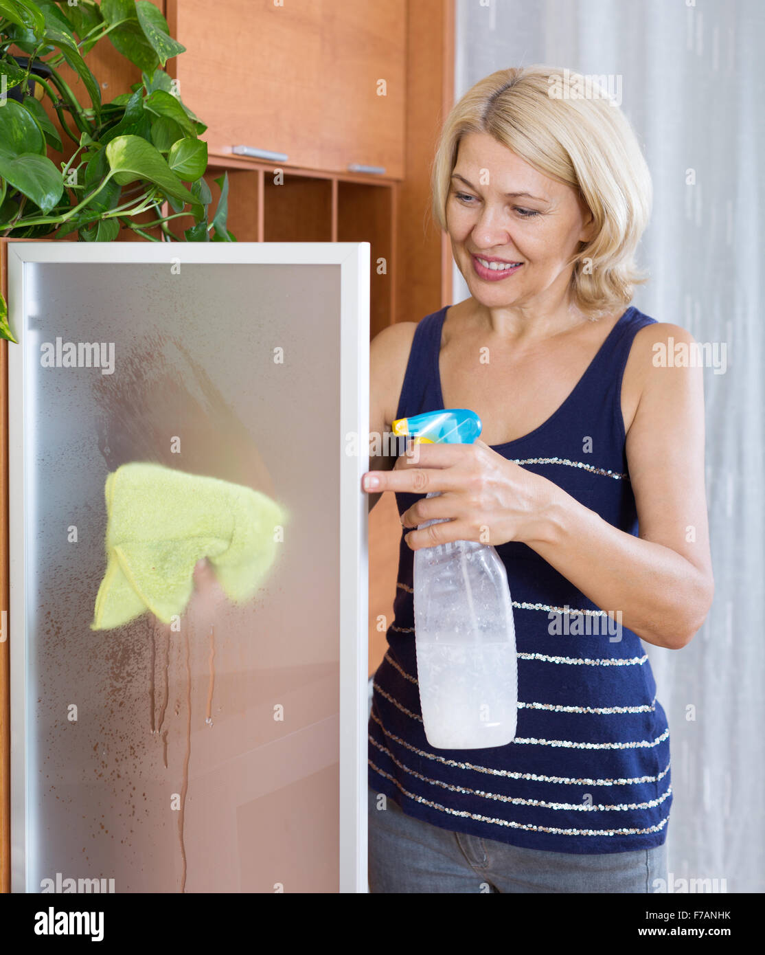 Smiling mature woman dusting glass of furniture at home Stock Photo - Alamy