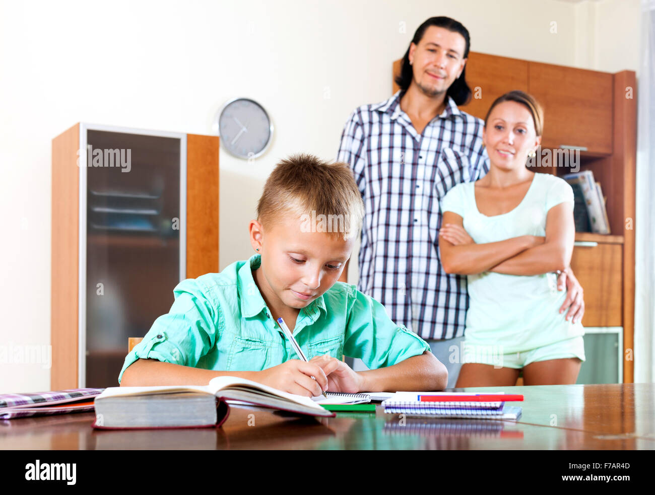 Smiling couple with schoolboy son doing homework in home interior Stock ...
