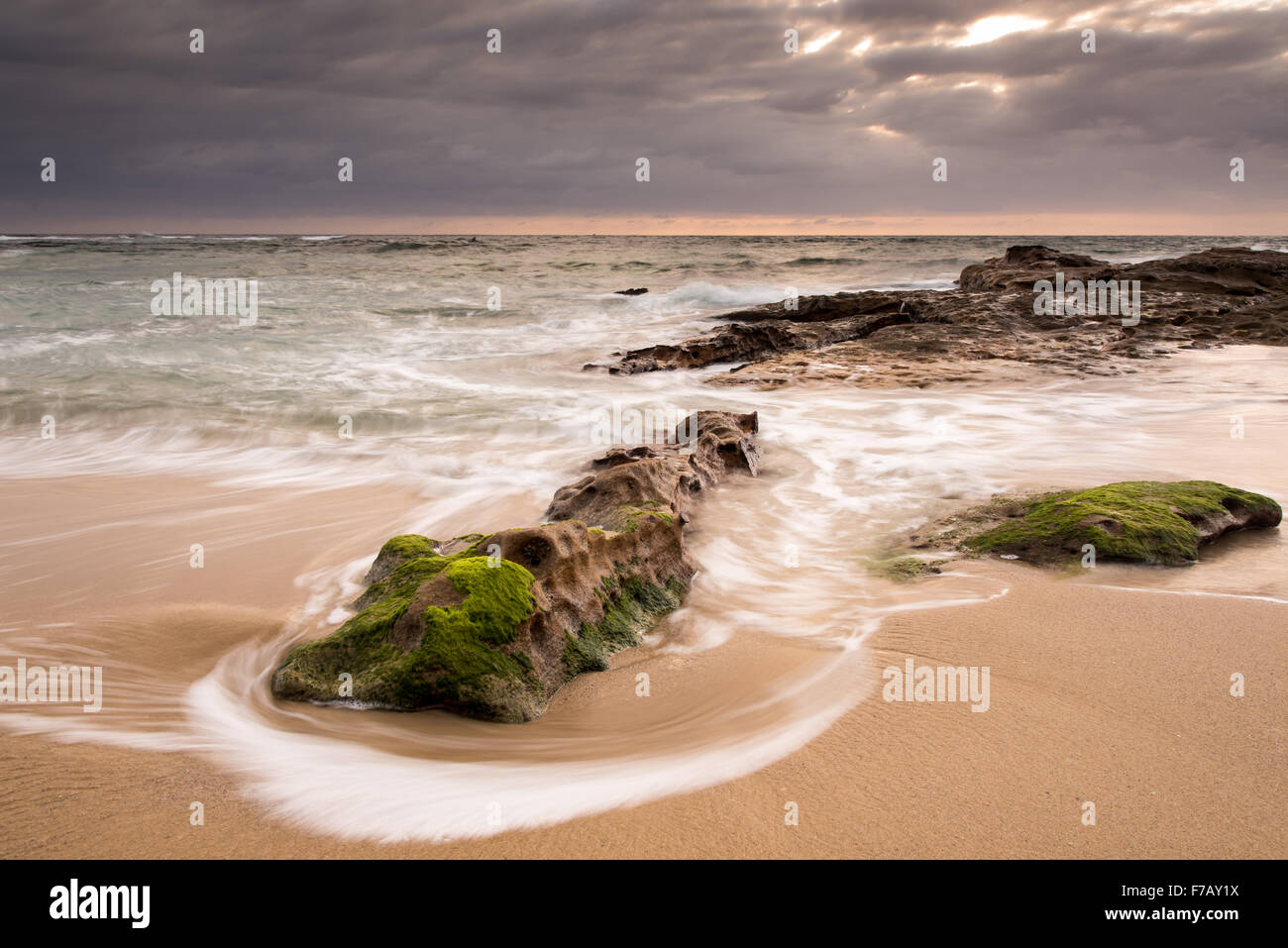 Waves flowing around a rock on a sandy beach Stock Photo - Alamy
