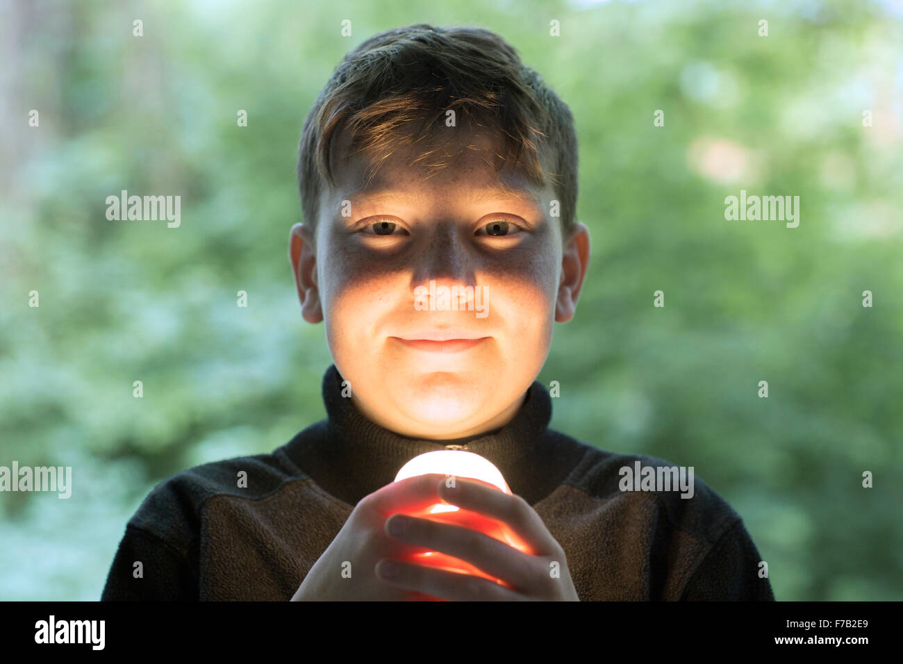 MODEL RELEASED. Boy holding a light bulb and illuminating his face ...