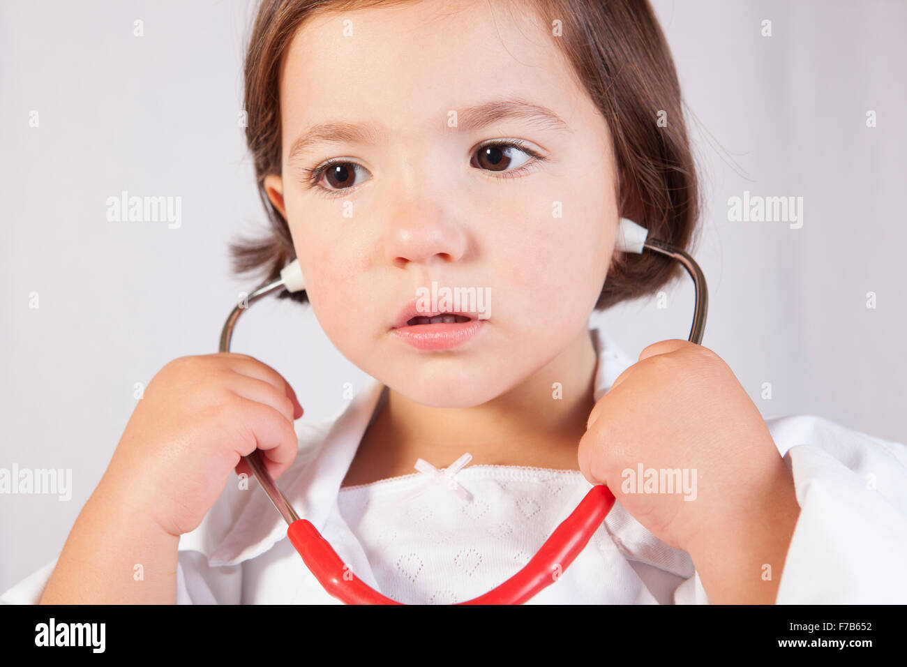 Little girl playing with a stethoscope. Isolated over white background ...