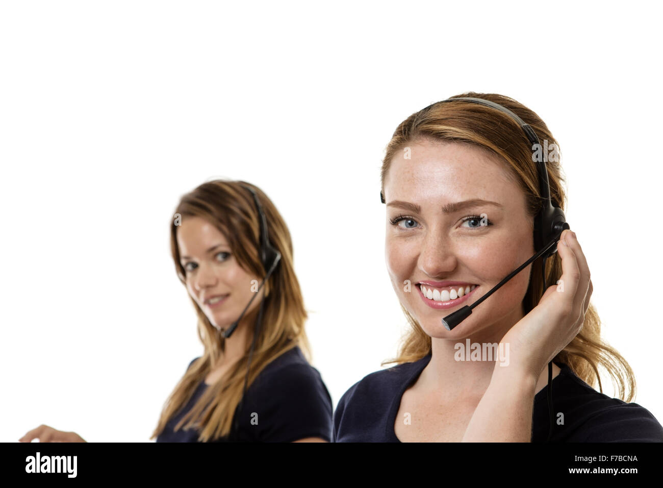two woman one standing in front in focus wearing a heand set talking ...