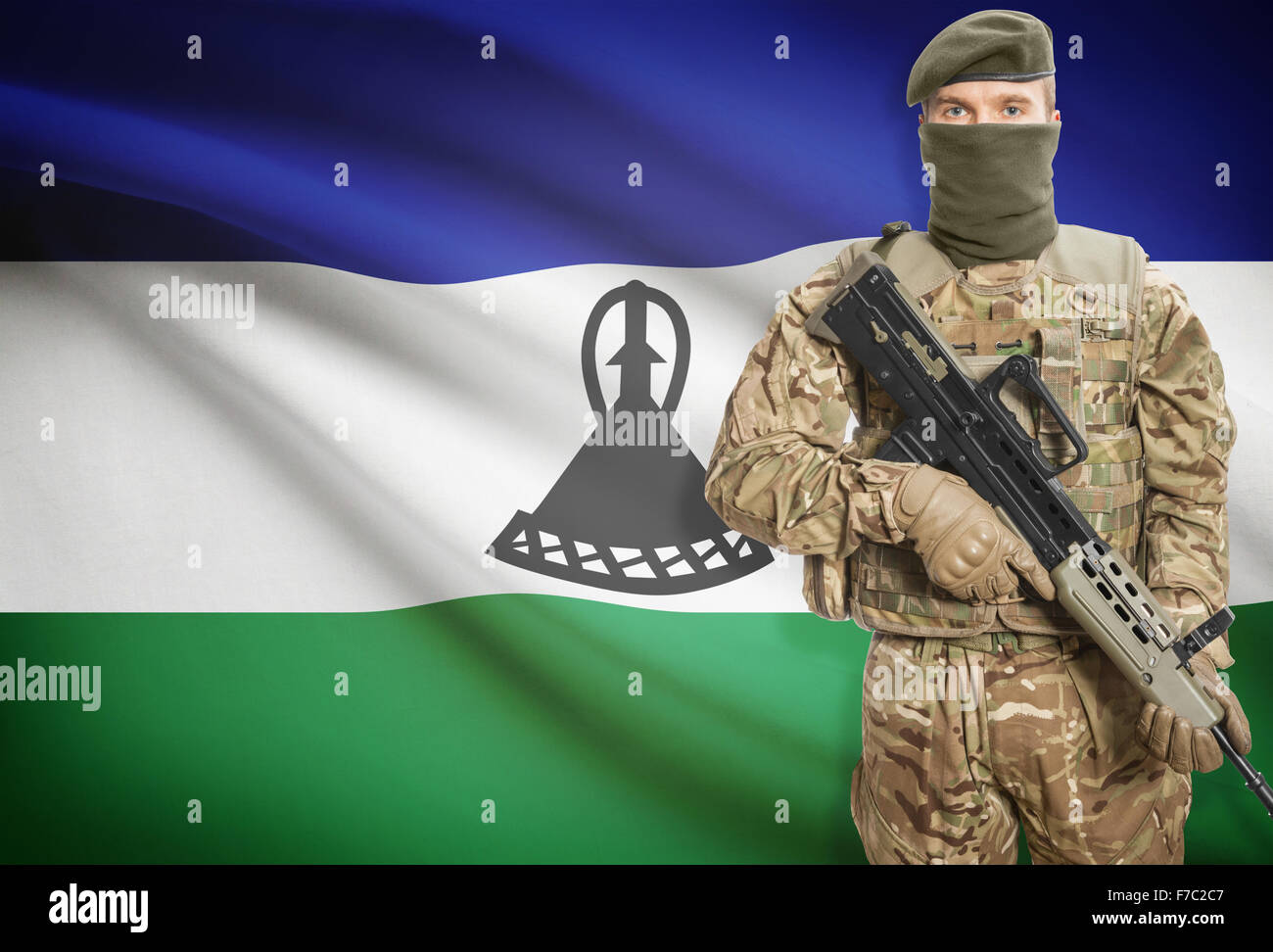 Soldier holding machine gun with national flag on background - Lesotho ...