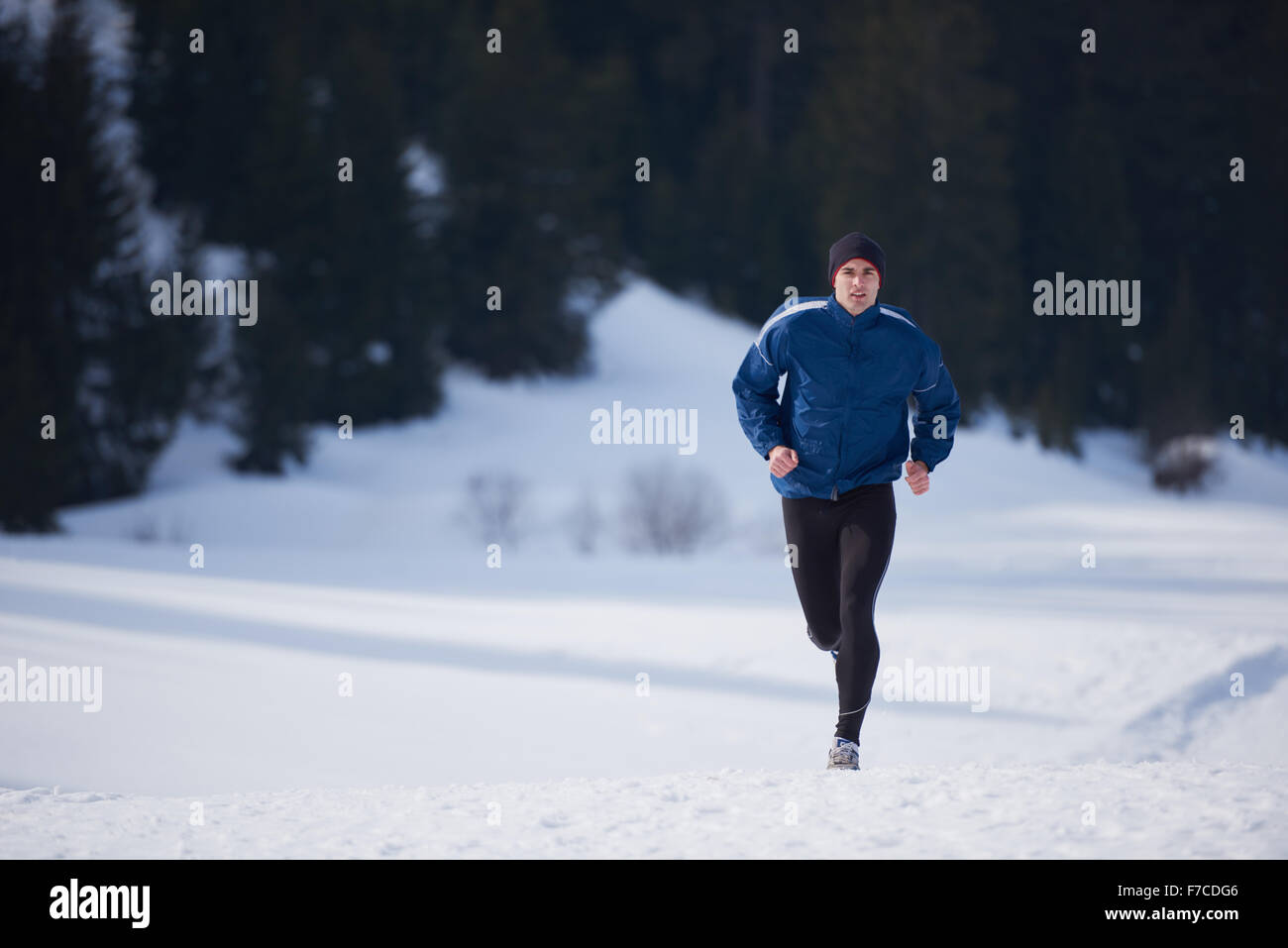 young man jogging on snow in forest, bautiful sunny winter day ...