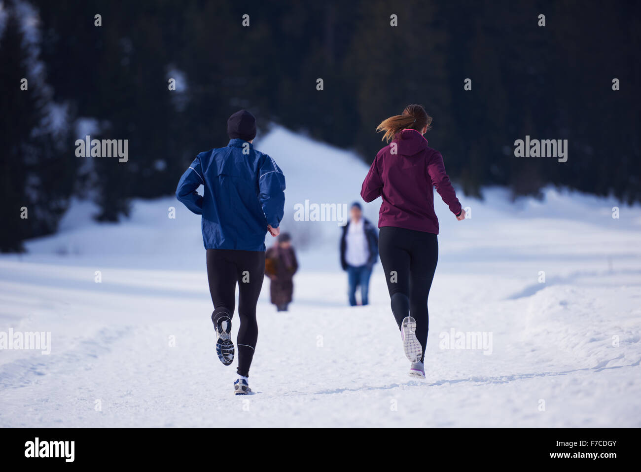 healthy young couple jogging outside on snow in forest. athlete running ...