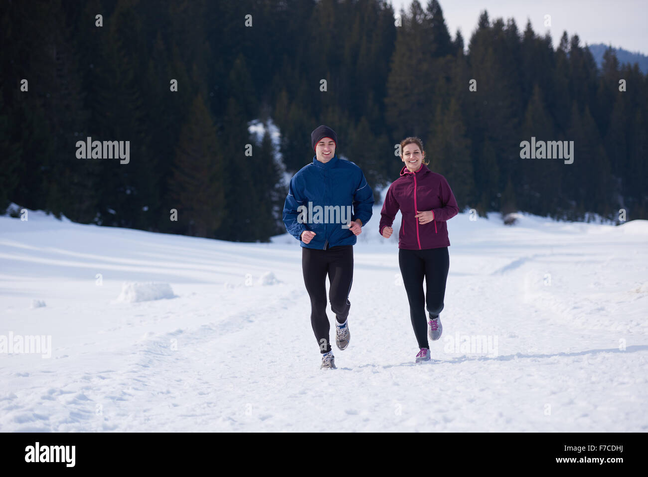 healthy young couple jogging outside on snow in forest. athlete running ...