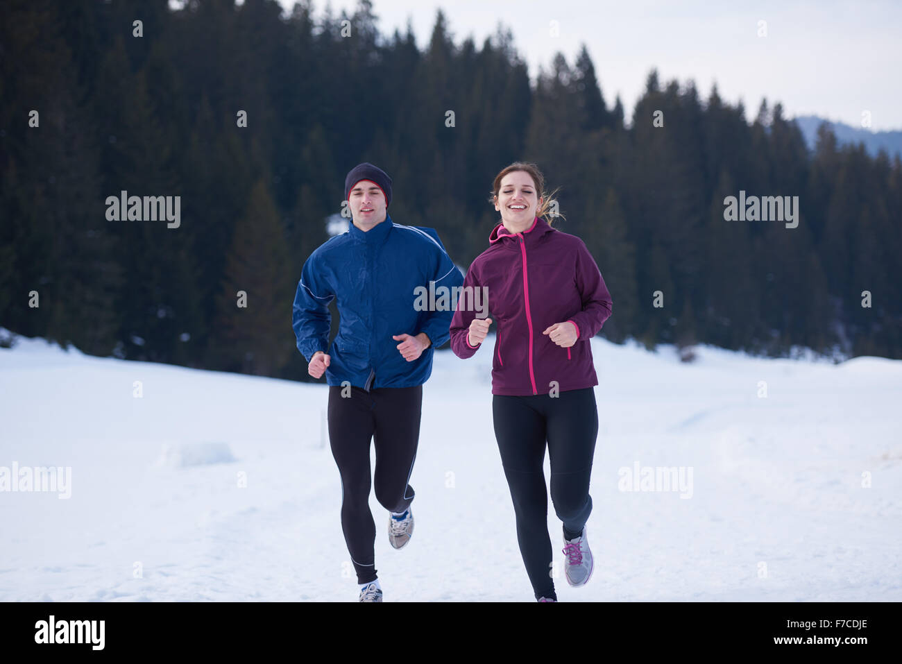 healthy young couple jogging outside on snow in forest. athlete running ...