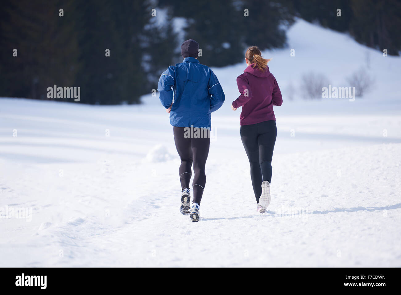 healthy young couple jogging outside on snow in forest. athlete running ...