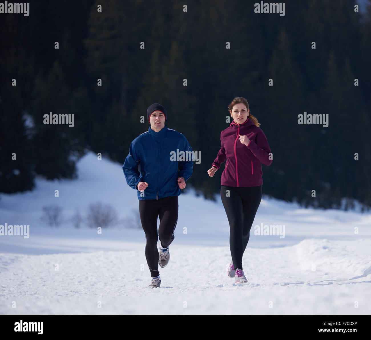 healthy young couple jogging outside on snow in forest. athlete running ...