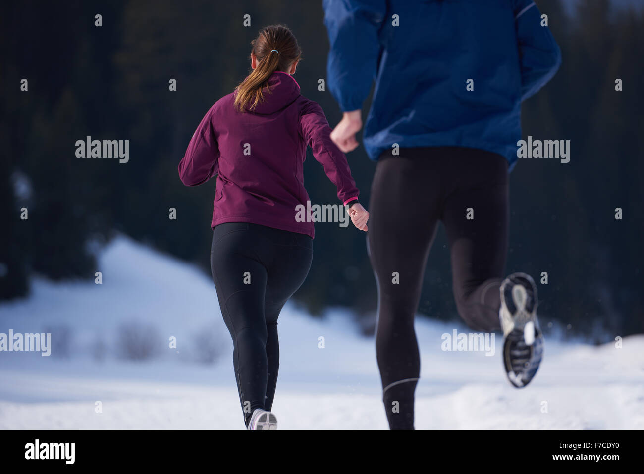 healthy young couple jogging outside on snow in forest. athlete running ...