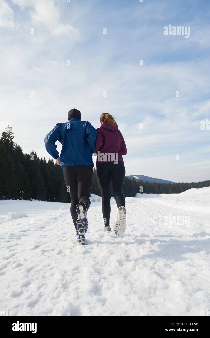 healthy young couple jogging outside on snow in forest. athlete running ...