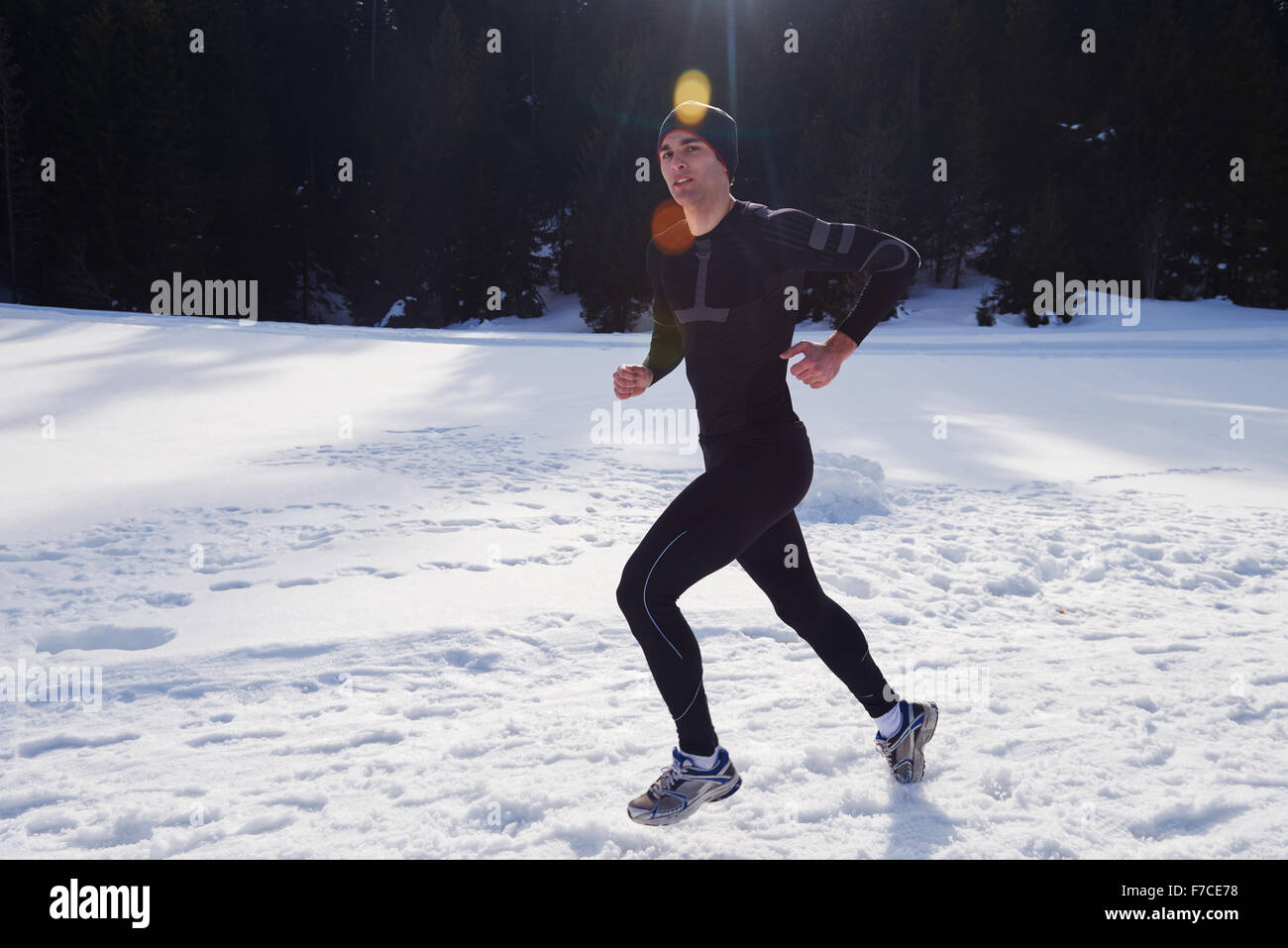 young man jogging on snow in forest, bautiful sunny winter day ...