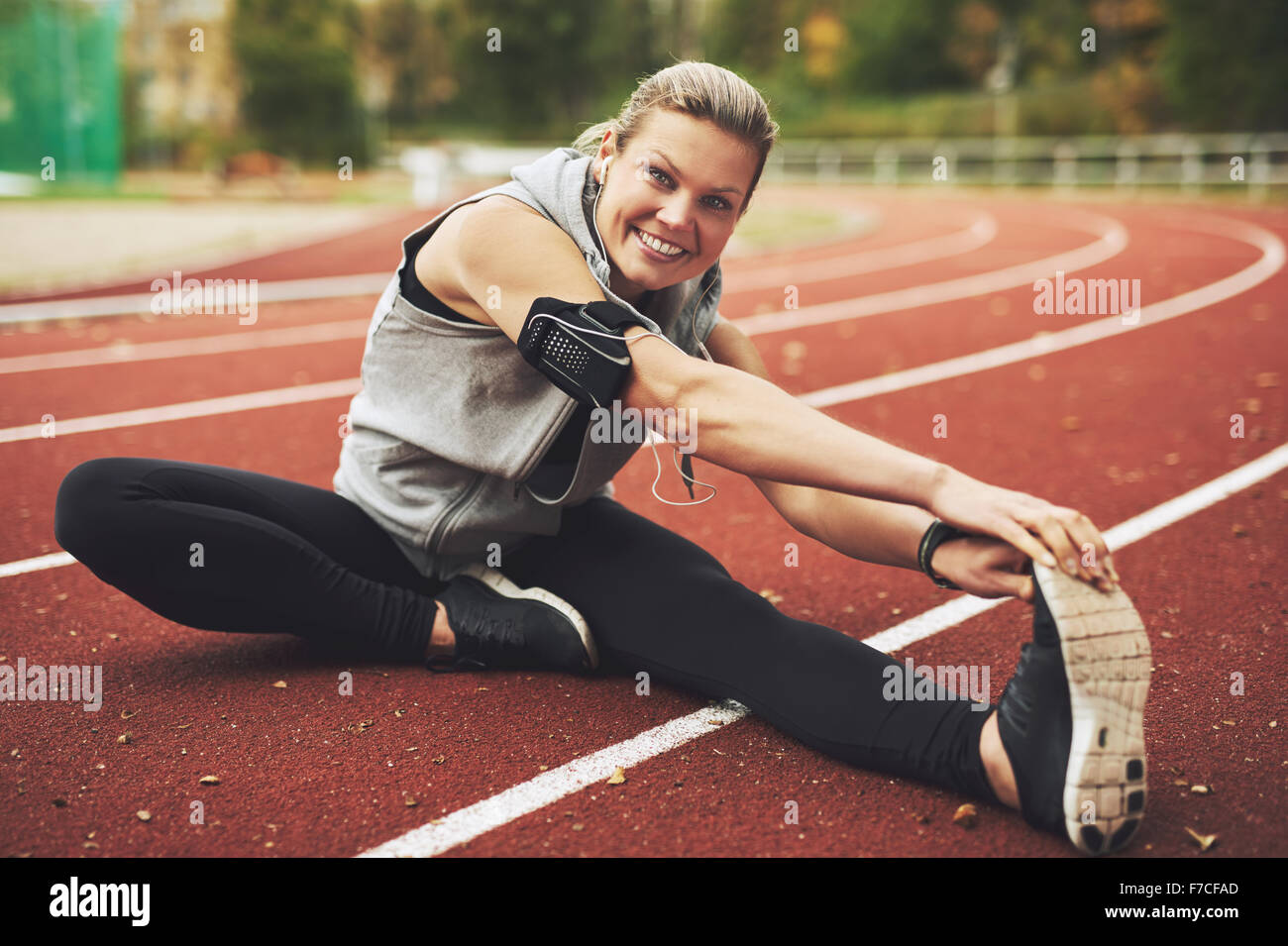 Young sportswoman sitting and stretching on track field while listening ...