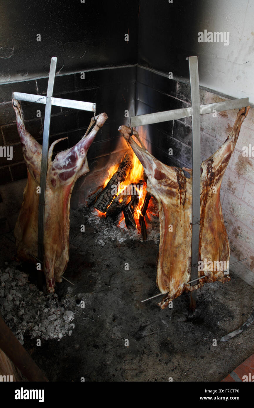 Asado barbecue. Lamb being roasted on a metal crucifix over and open ...