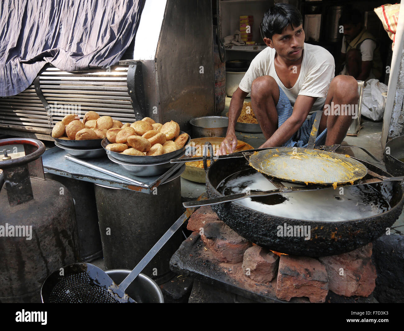 Market Trader crouches down whilst preparing a batch of street food ...