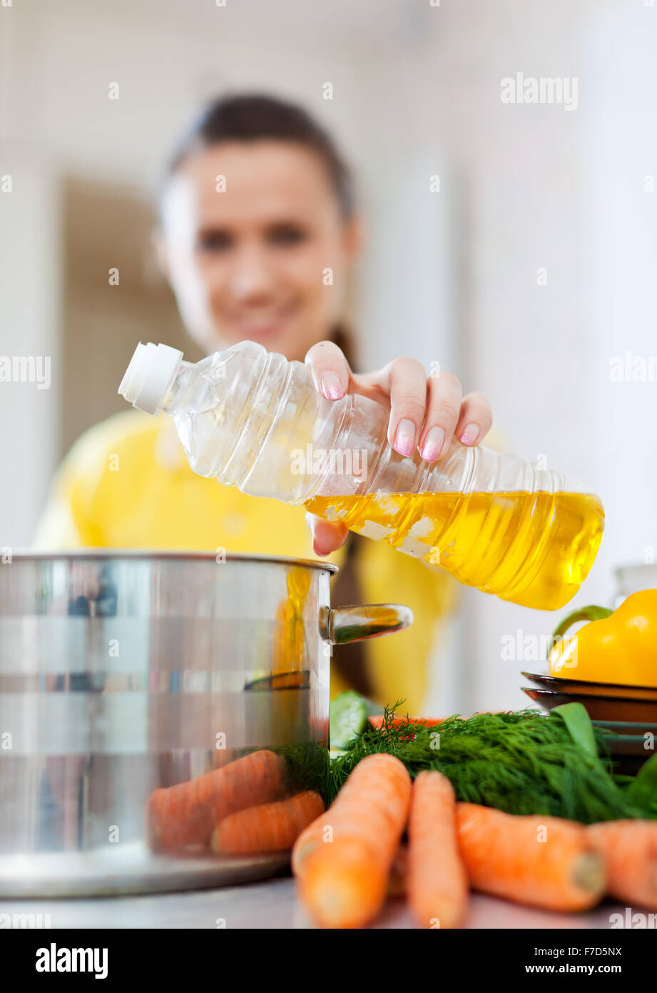 Woman pouring oil from bottle into the saucepan. Focus on hand with ...